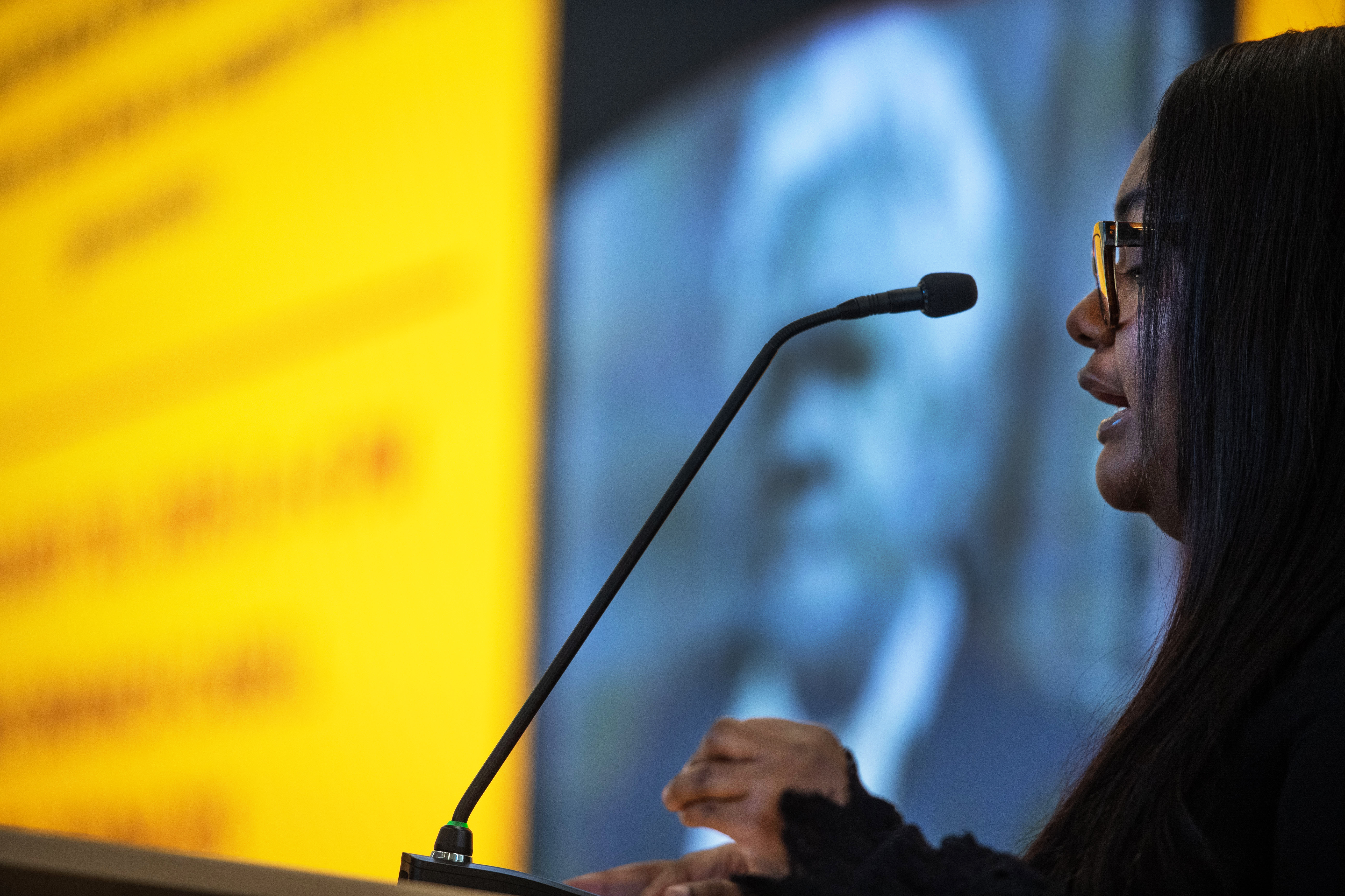 Shakiah Bonipart speaks at a podium with a microphone. Behind her, a ...