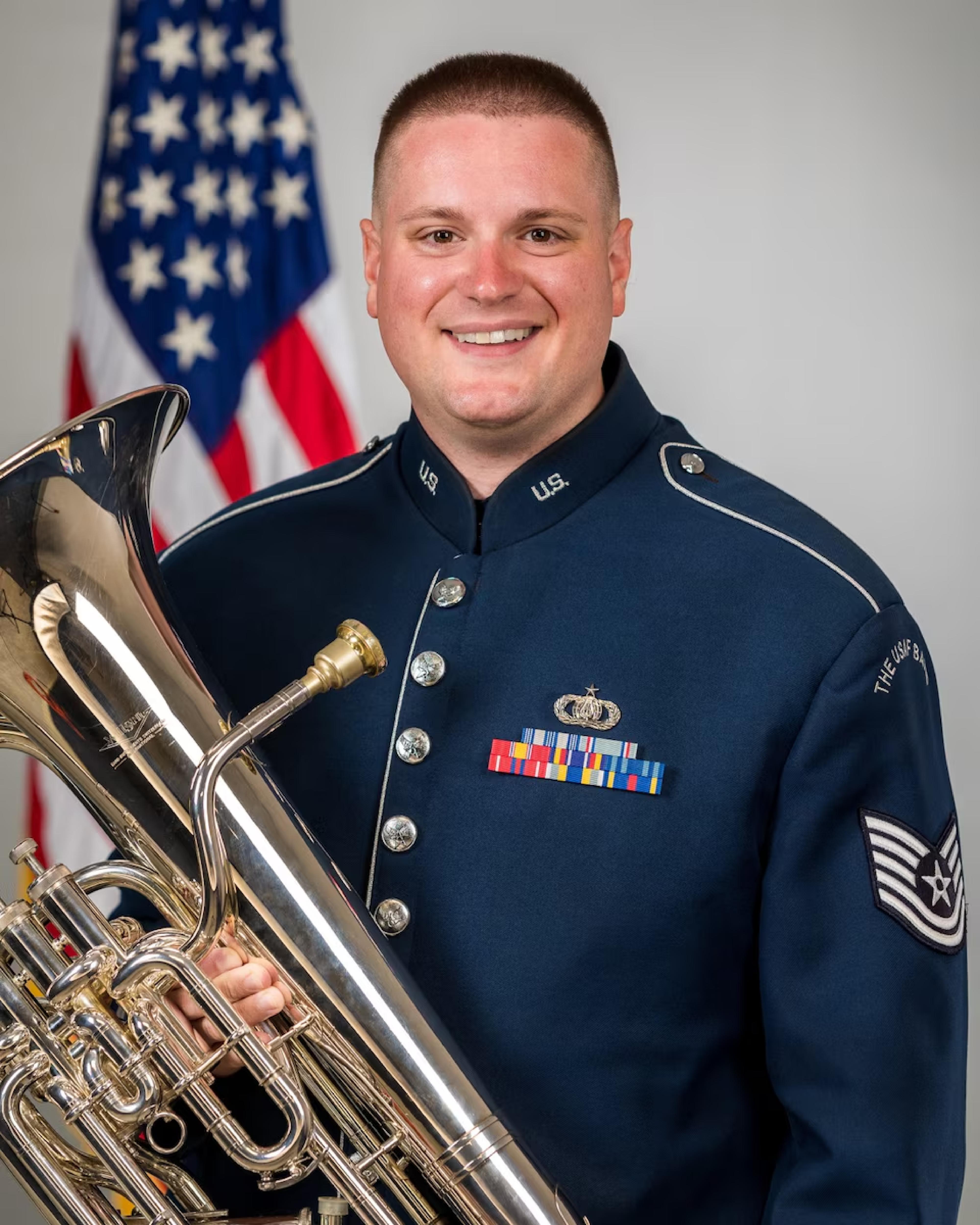 Smiling man in Air Force Band uniform holds a tuba. The uniform is dark ...