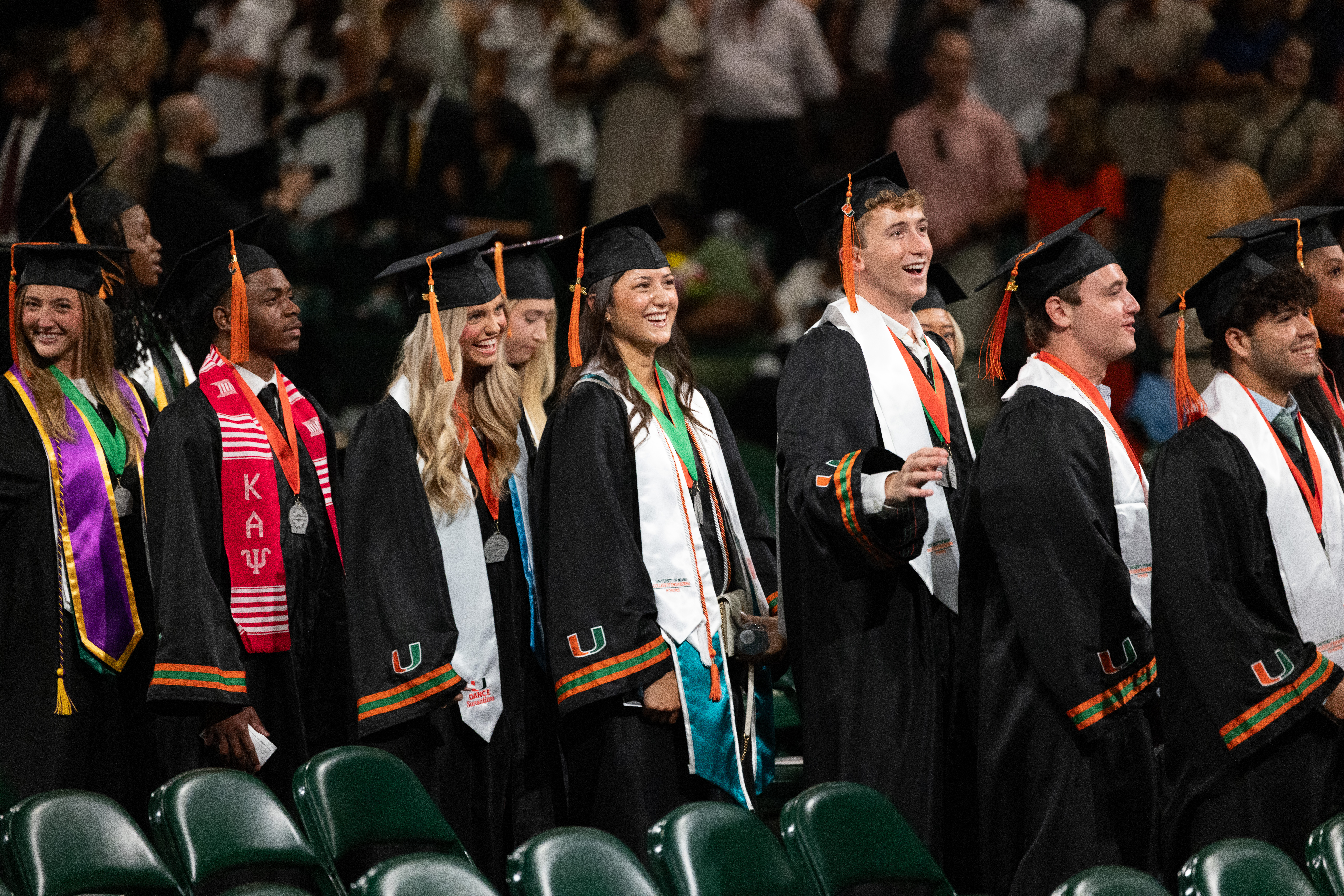 Graduates in black gowns and caps stand in rows at the Spring 2026 ...