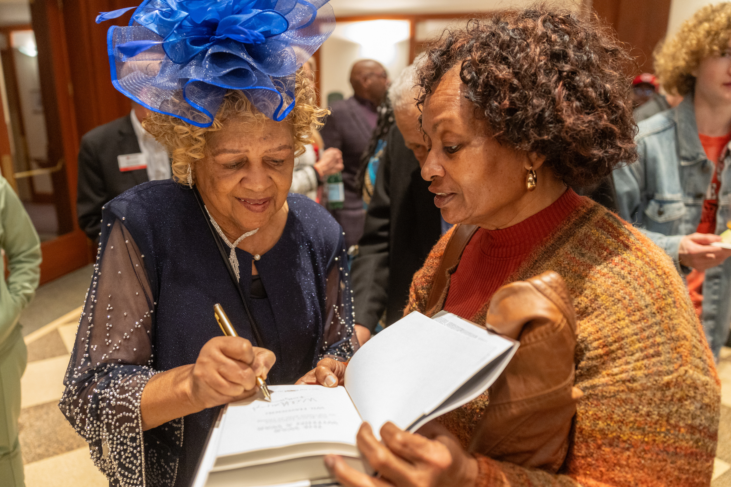 Wil Haygood signs a book at his book launch. A woman in a blue hat ...