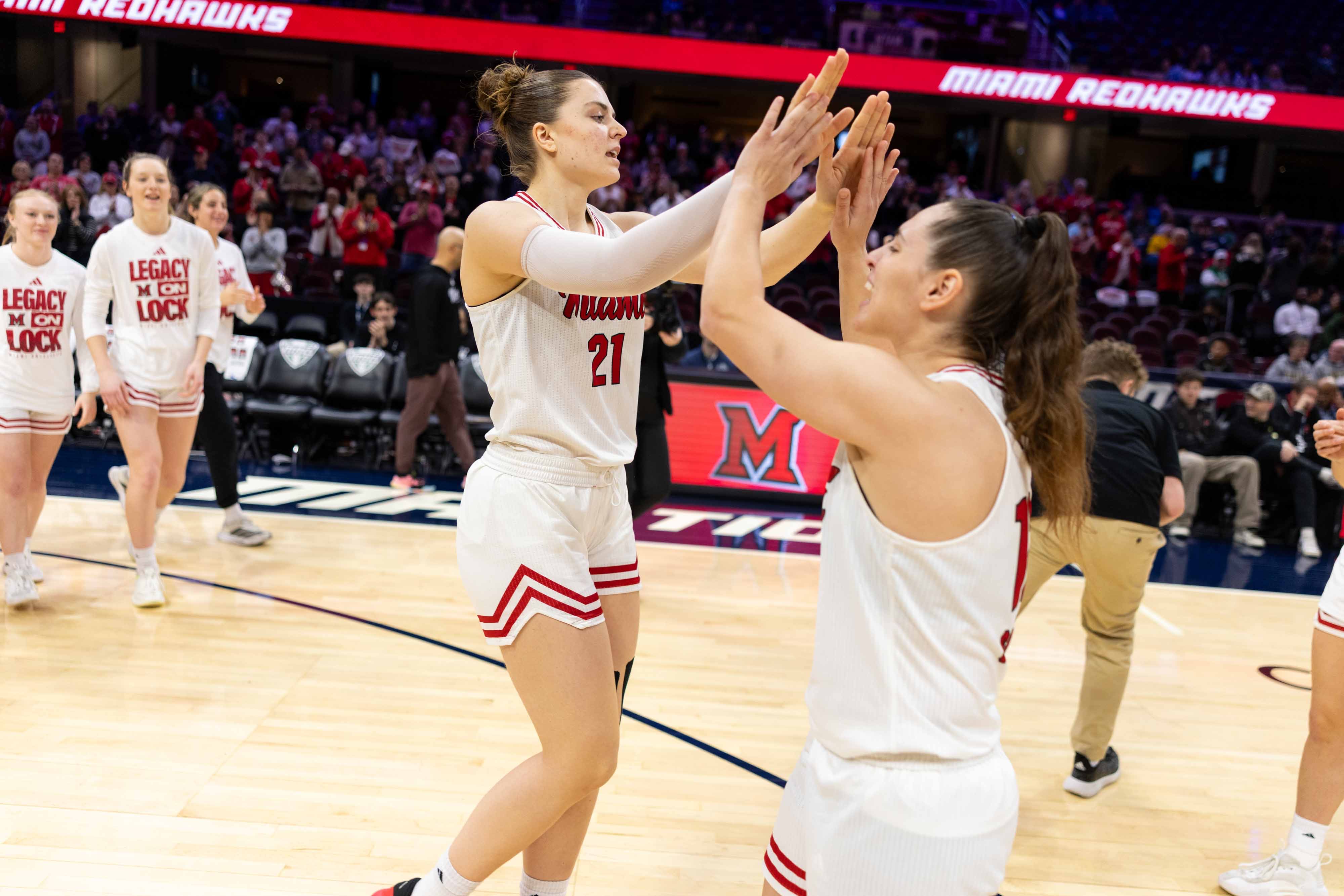 Two Miami Redhawks basketball players high-five on the court. They wear ...