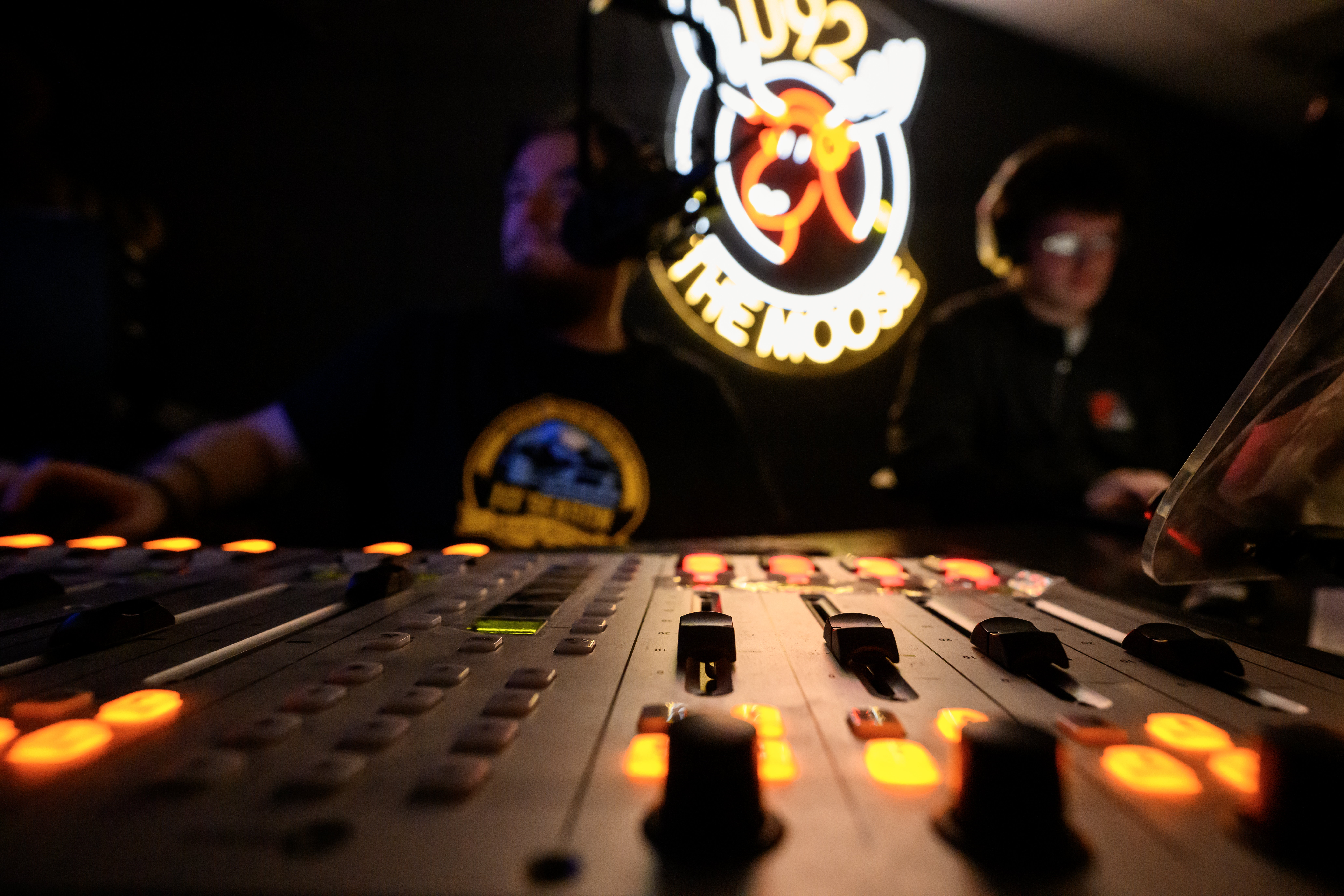 A mixing board with glowing orange lights and faders sits in a dimly ...
