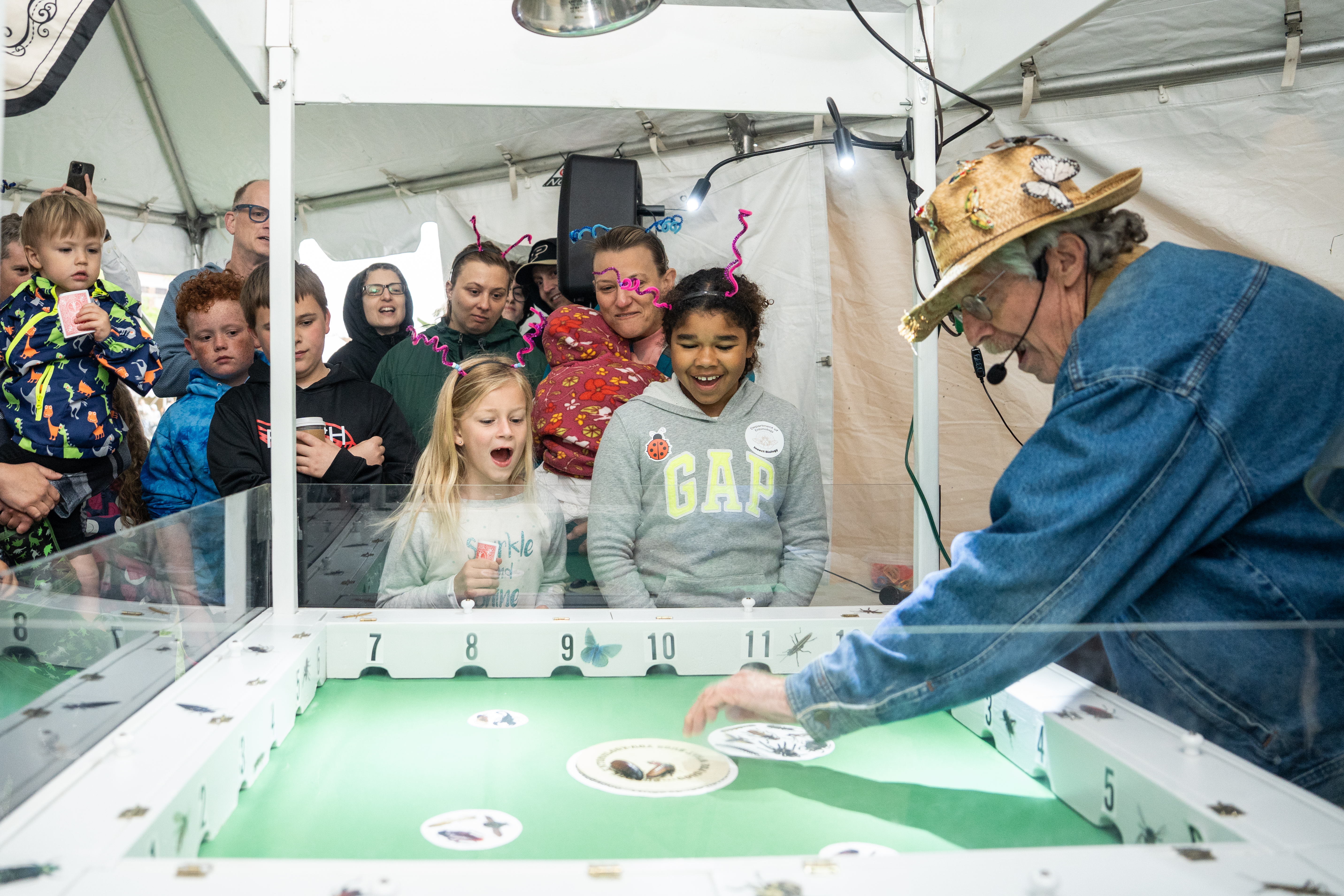 At Spring Fest, children watch a man in a butterfly-covered hat place ...
