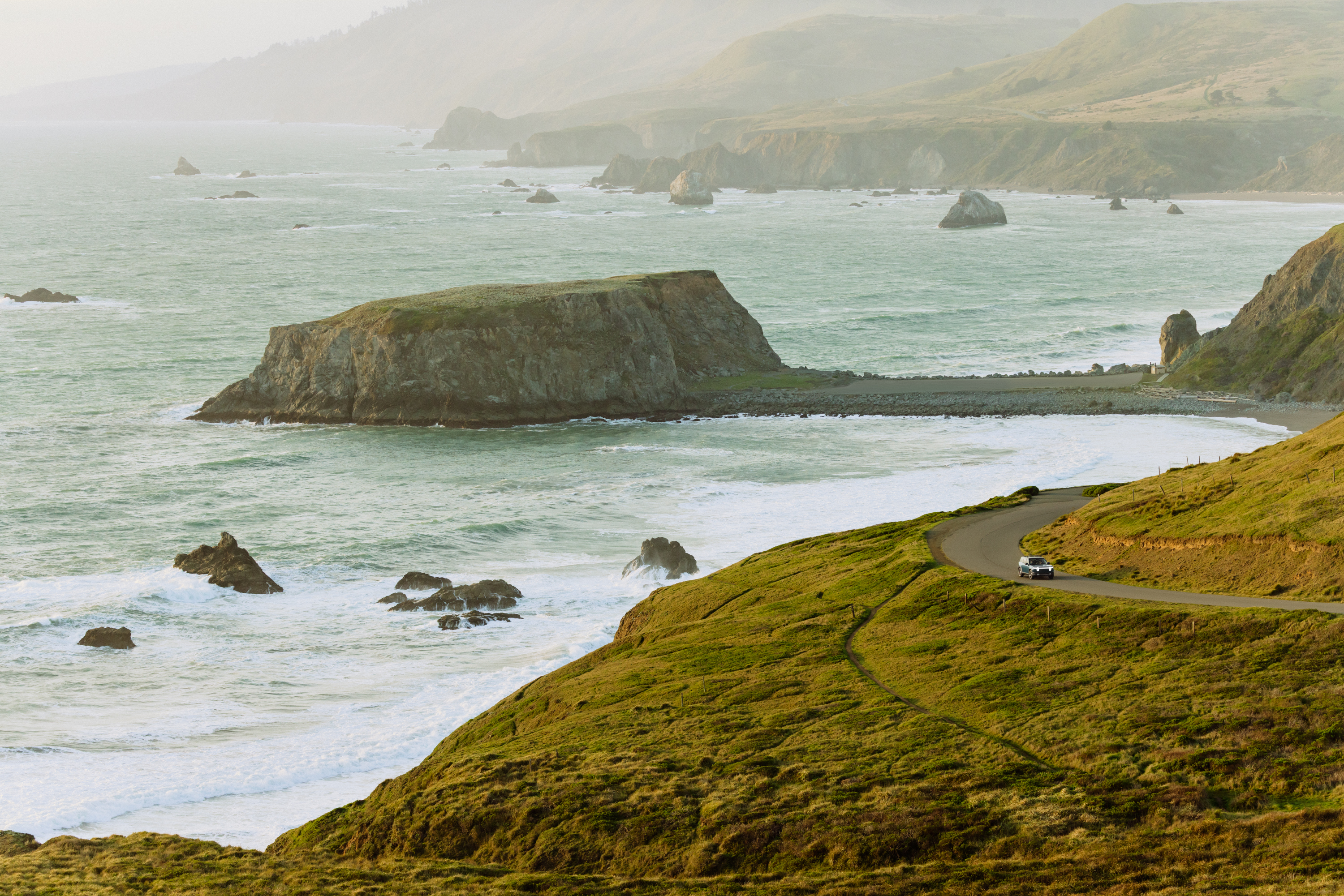Coastal view of a car driving on a winding road along a grassy hillside ...
