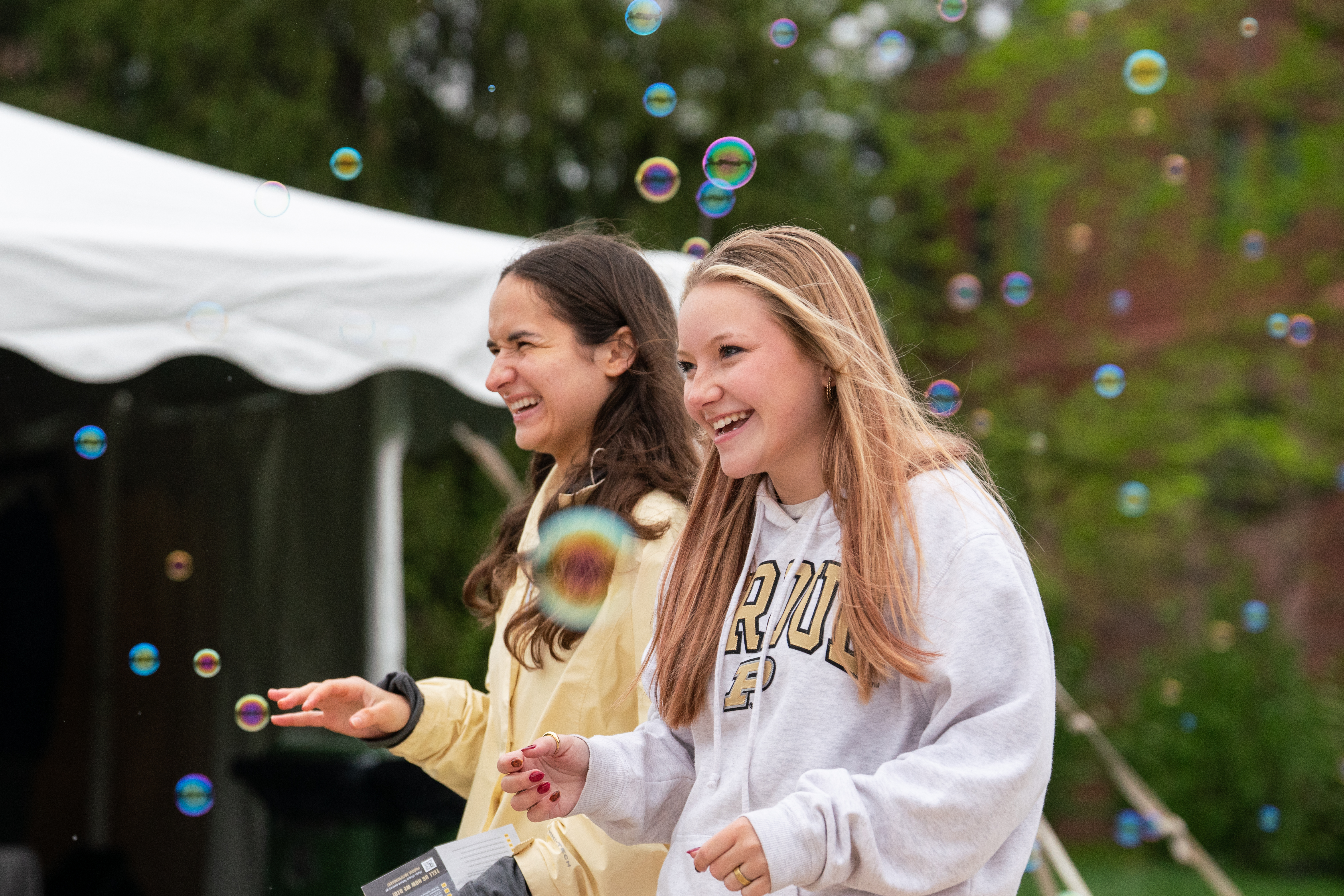 Two smiling women walk among floating bubbles at Spring Fest. One wears ...