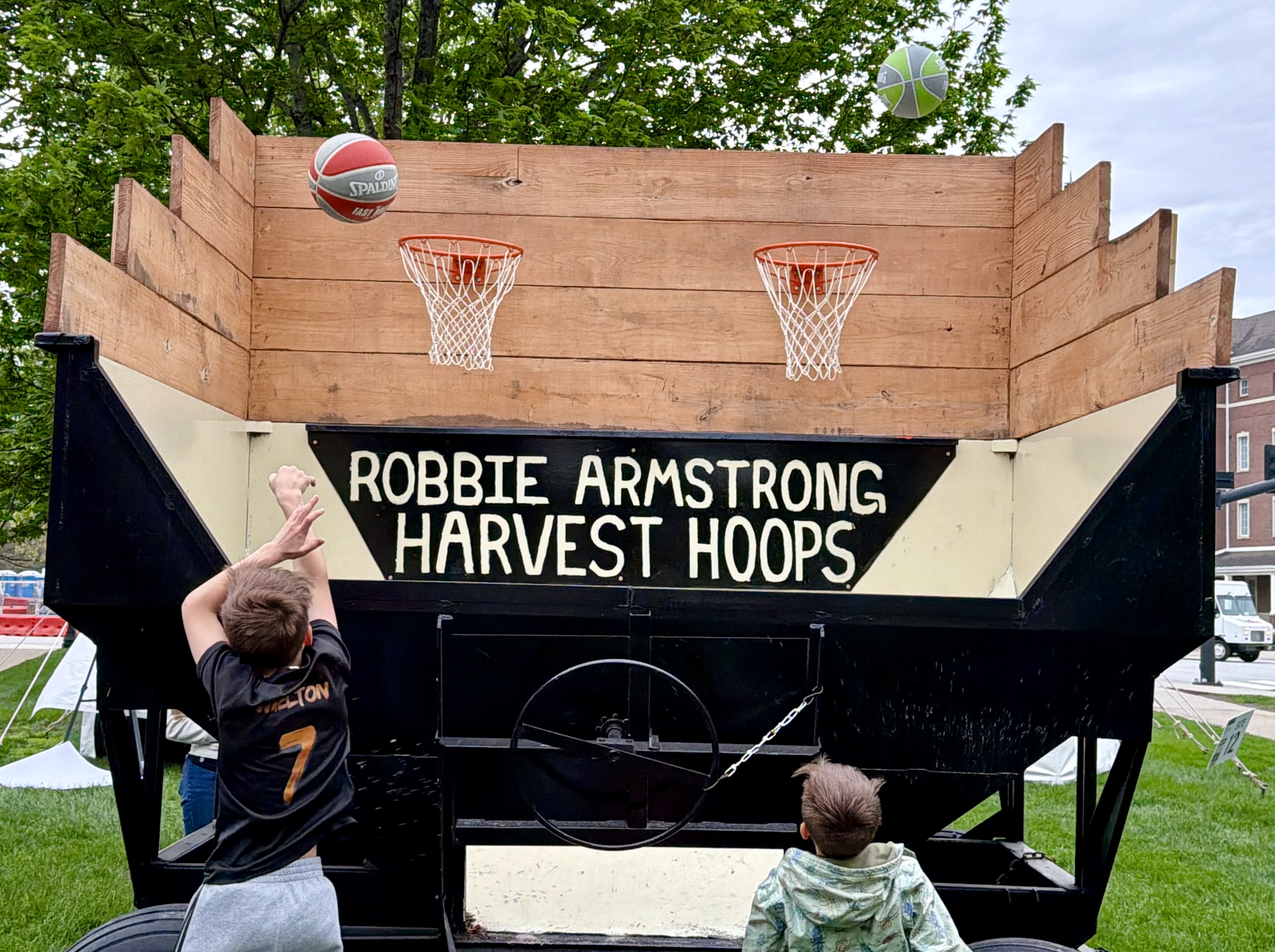 A boy shoots a basketball at a hoop mounted on a wagon labeled