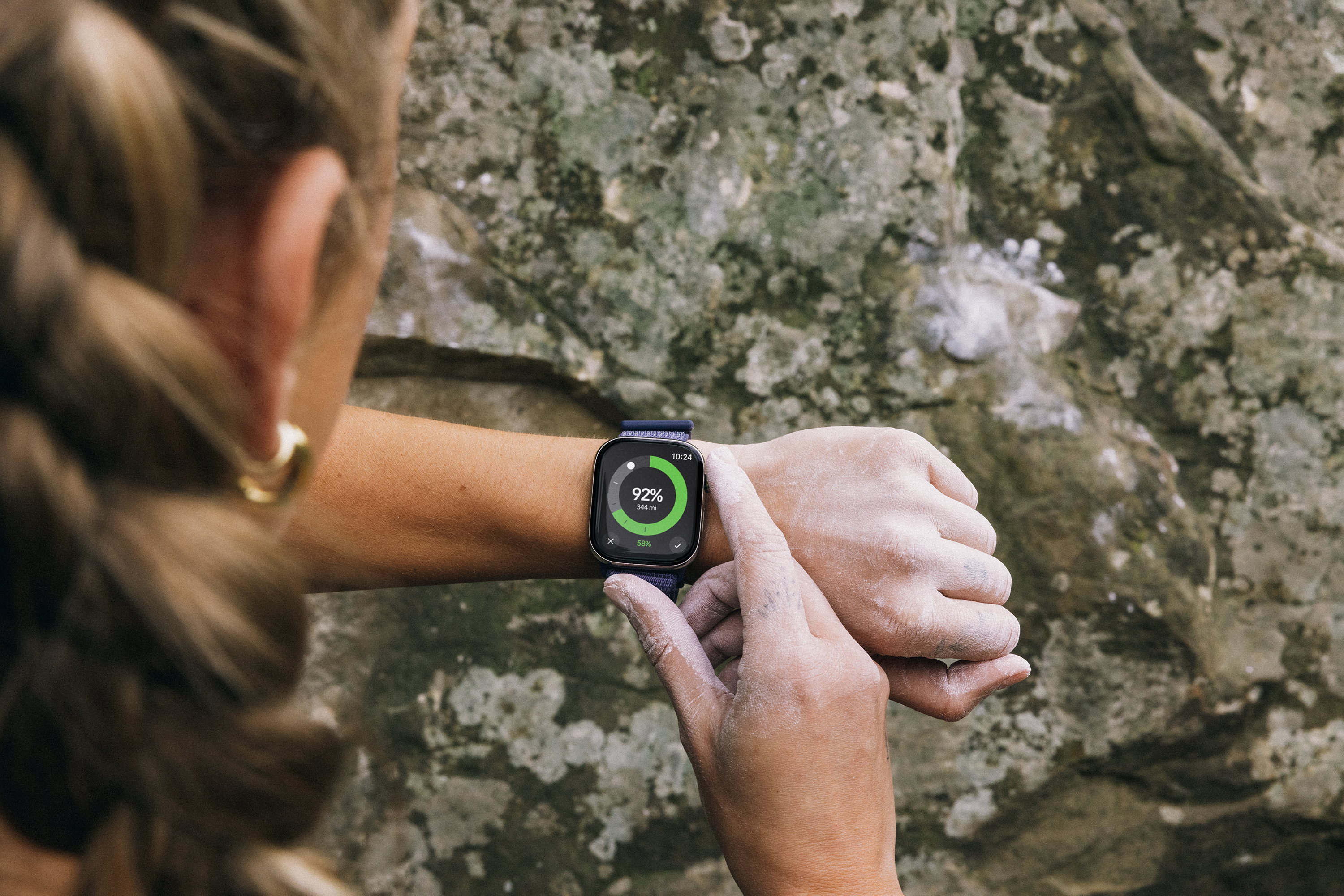 Climber checks smartwatch against rock wall. The watch face displays