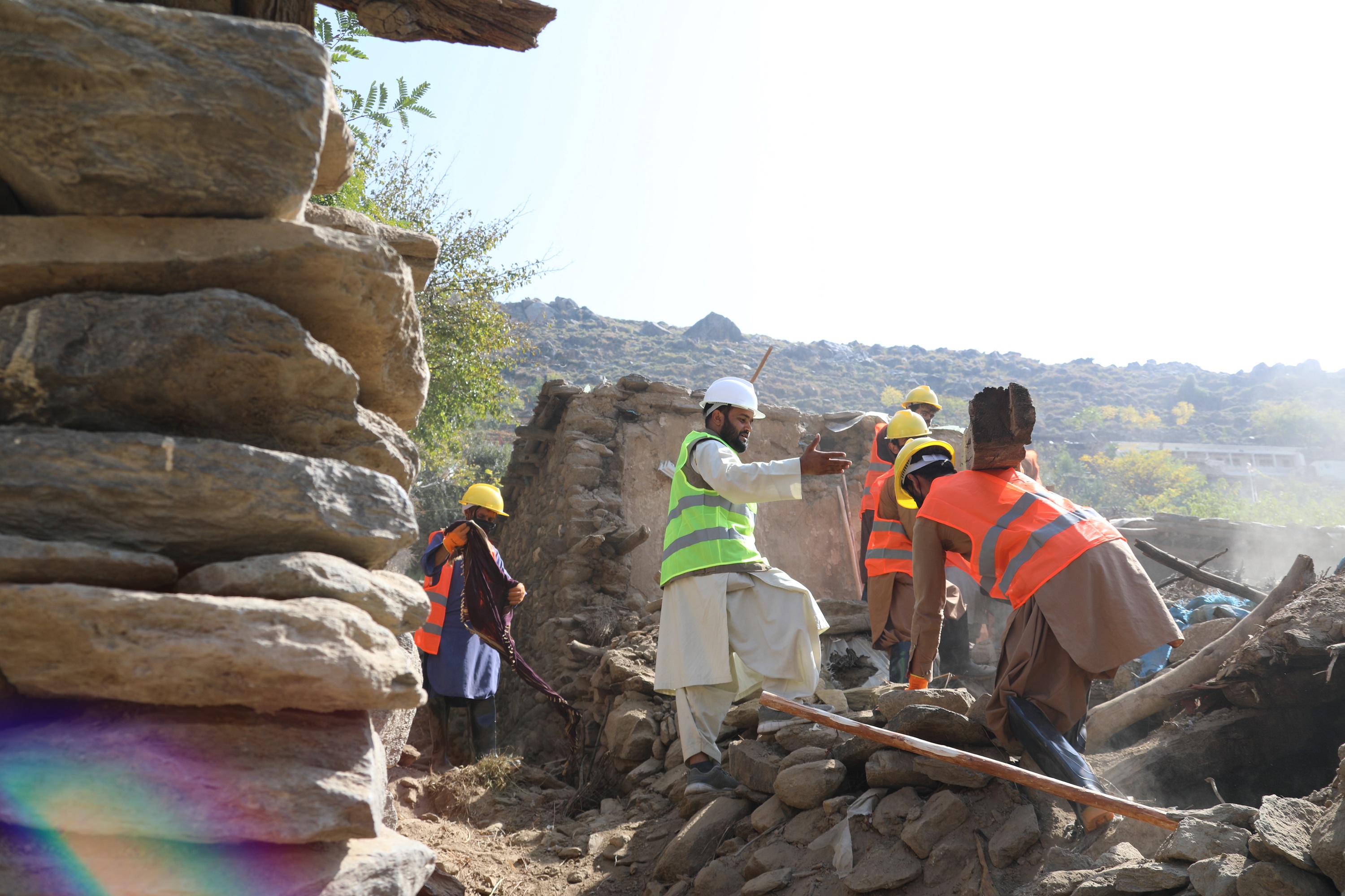 Rescue workers in hard hats and vests search through rubble in a rural ...