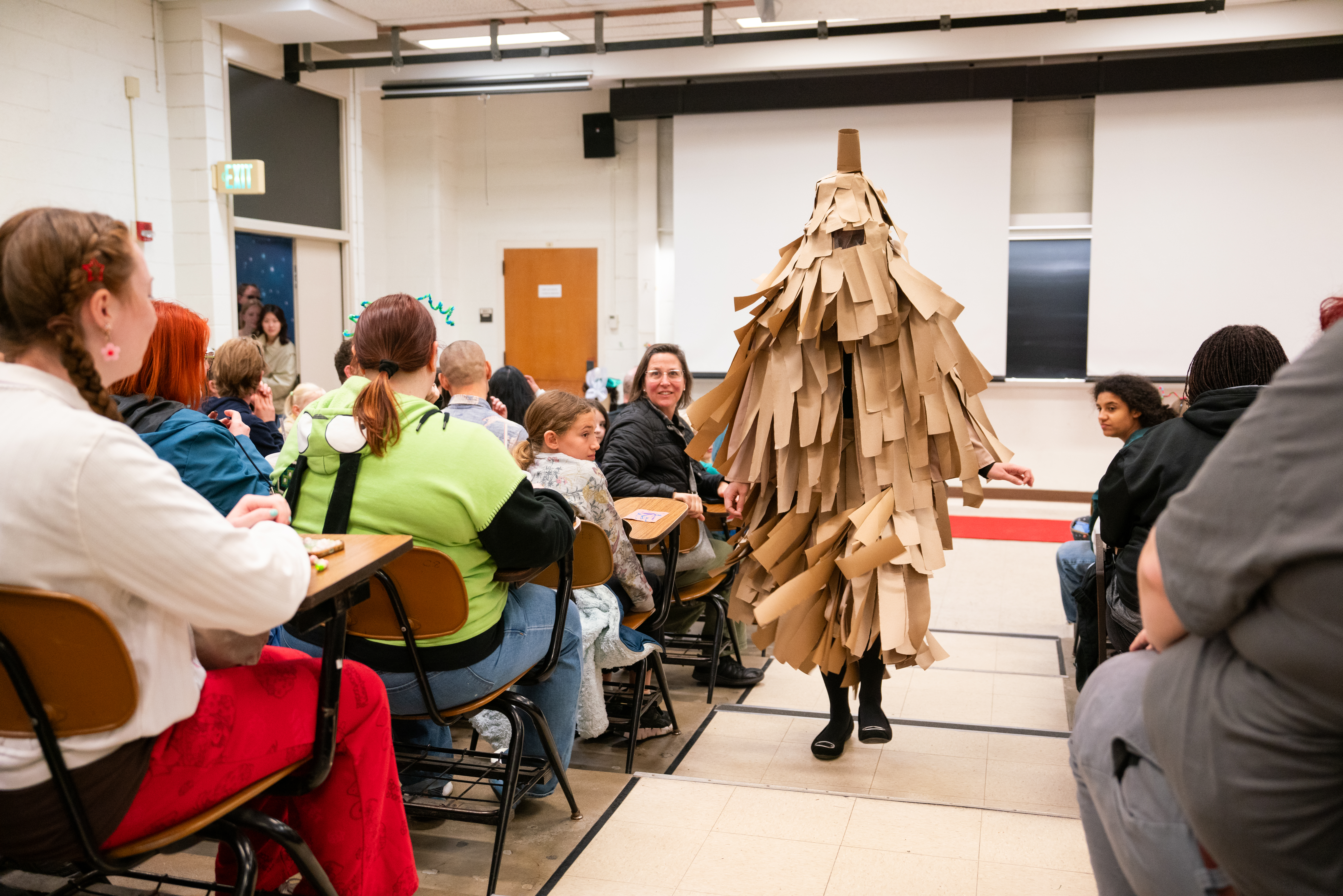 A person in a costume made of brown paper walks in front of an audience ...