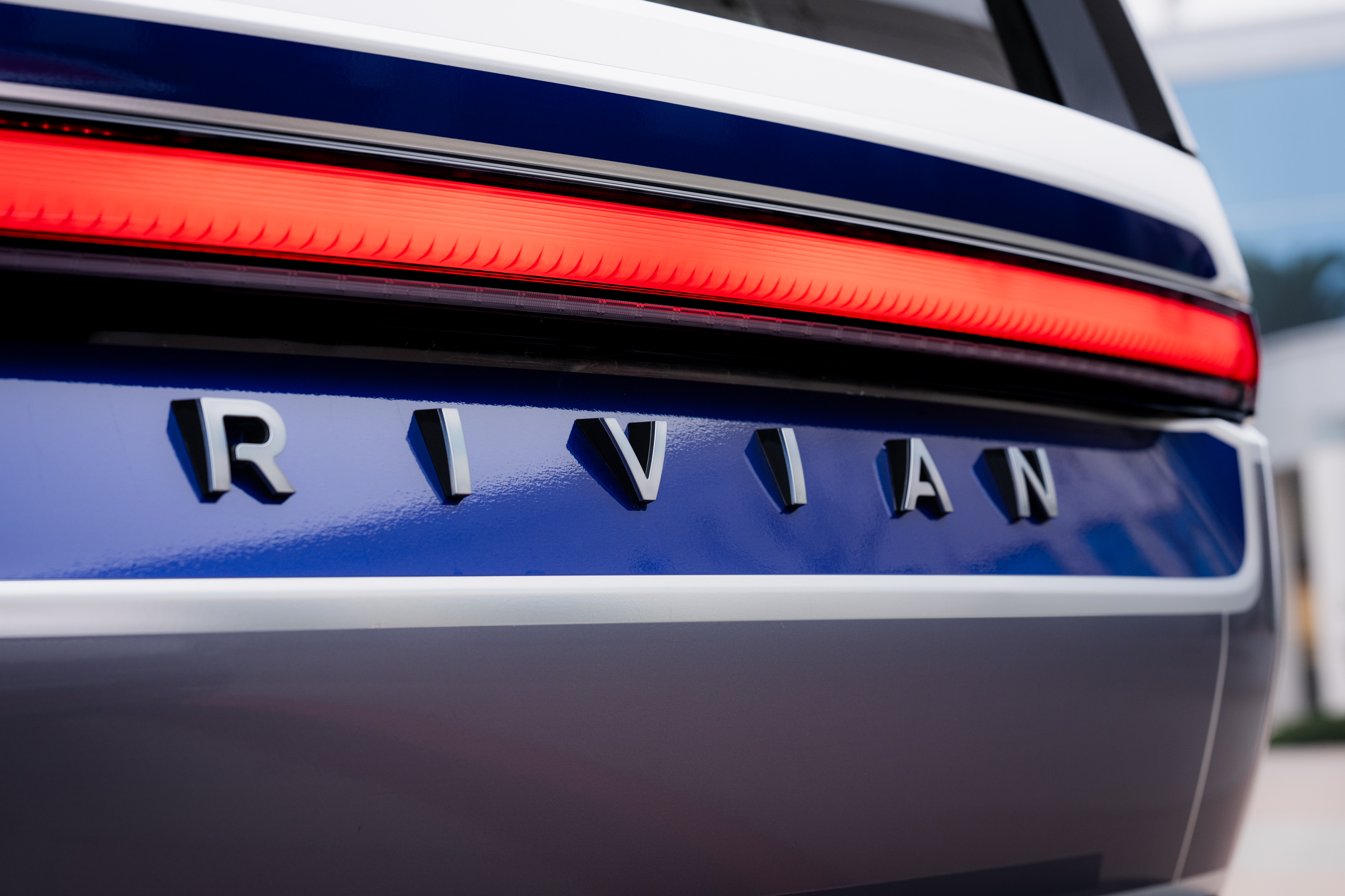 Close-up of the rear of a blue Rivian vehicle, showing the illuminated ...