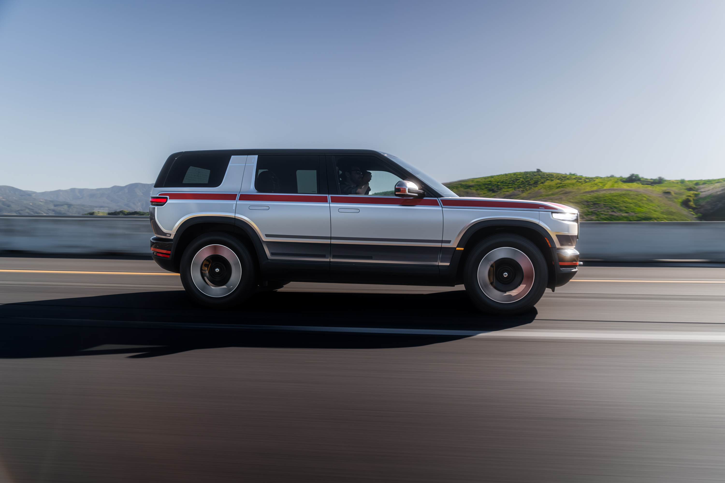 Silver SUV with a red stripe drives on a highway. Motion blur suggests ...