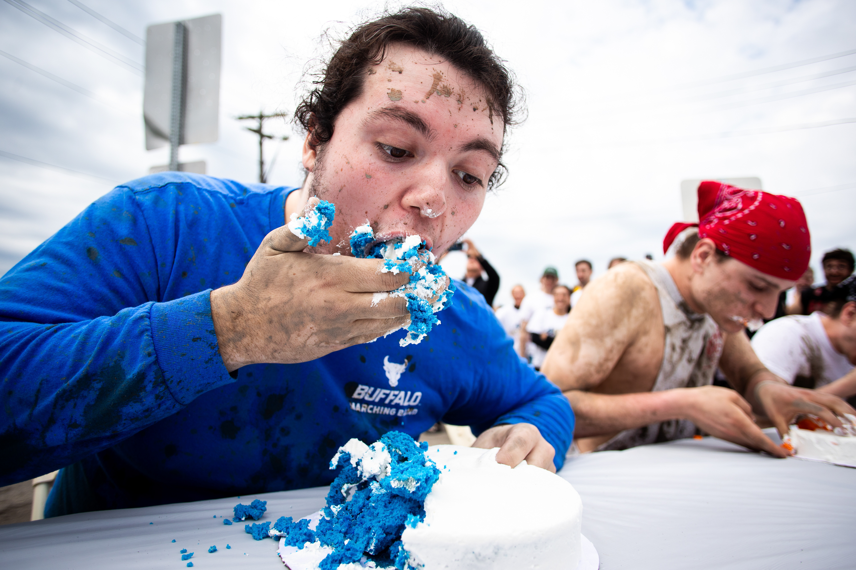 A person stuffs blue cake into their mouth during a cake eating contest.