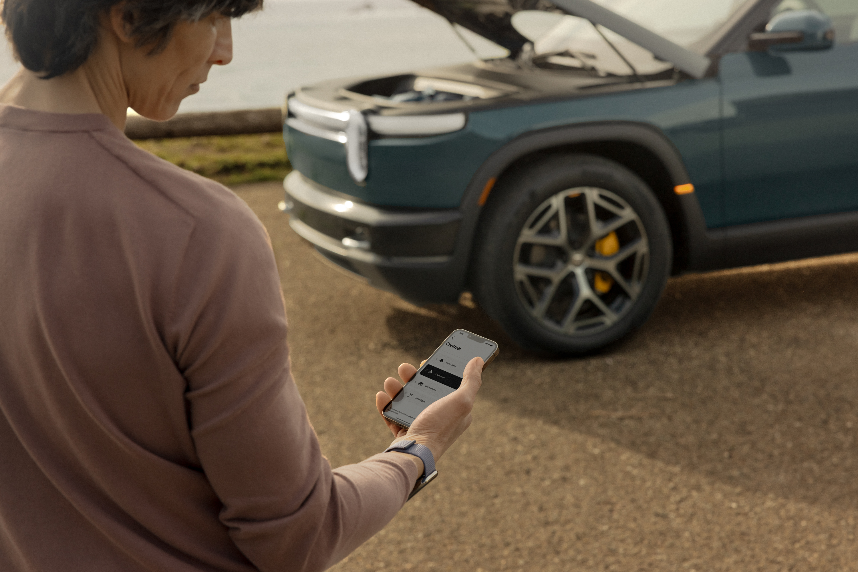 Person uses a smartphone app to control a dark green Rivian truck with ...
