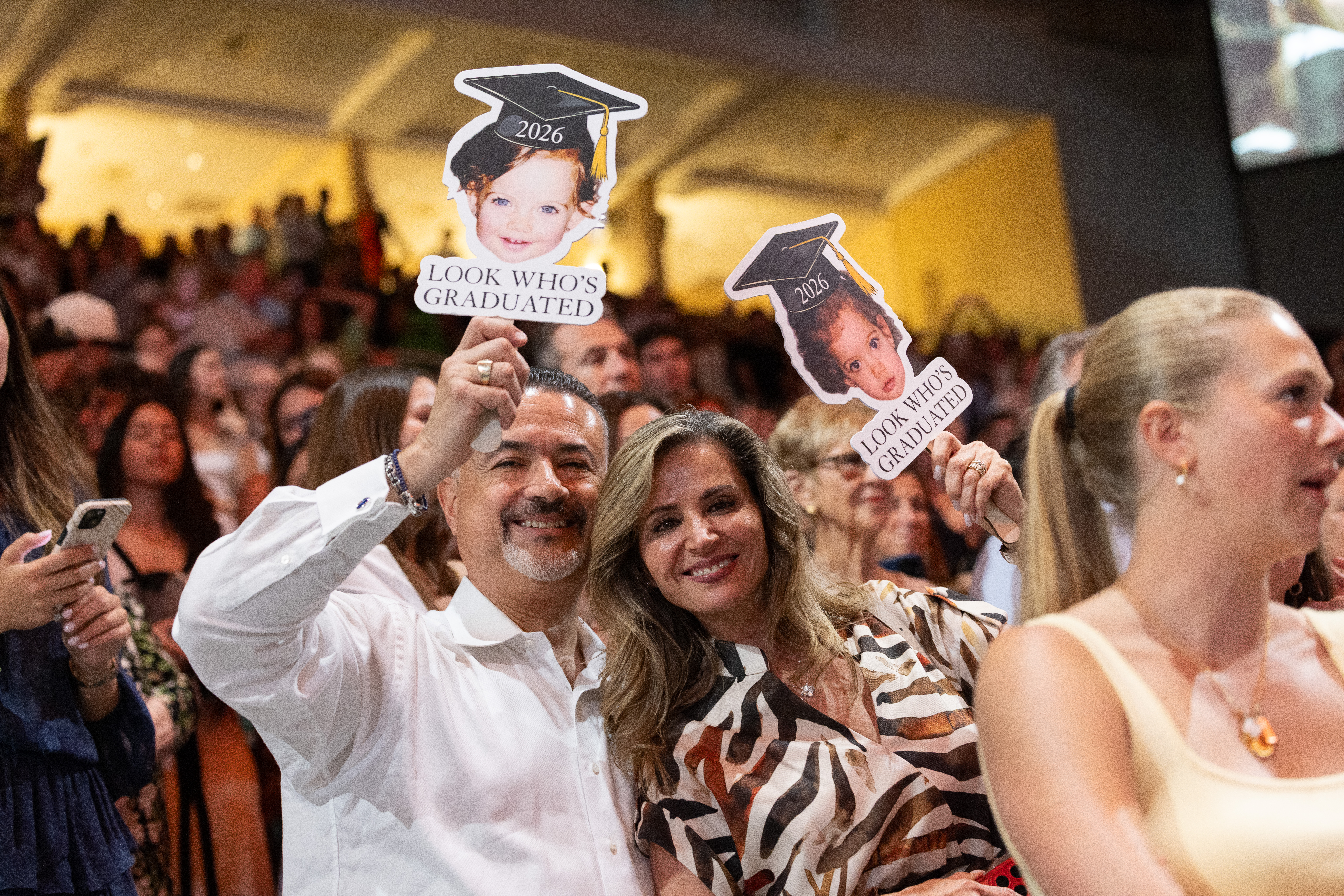 Parents at the 2026 Commencement hold signs with baby photos wearing ...