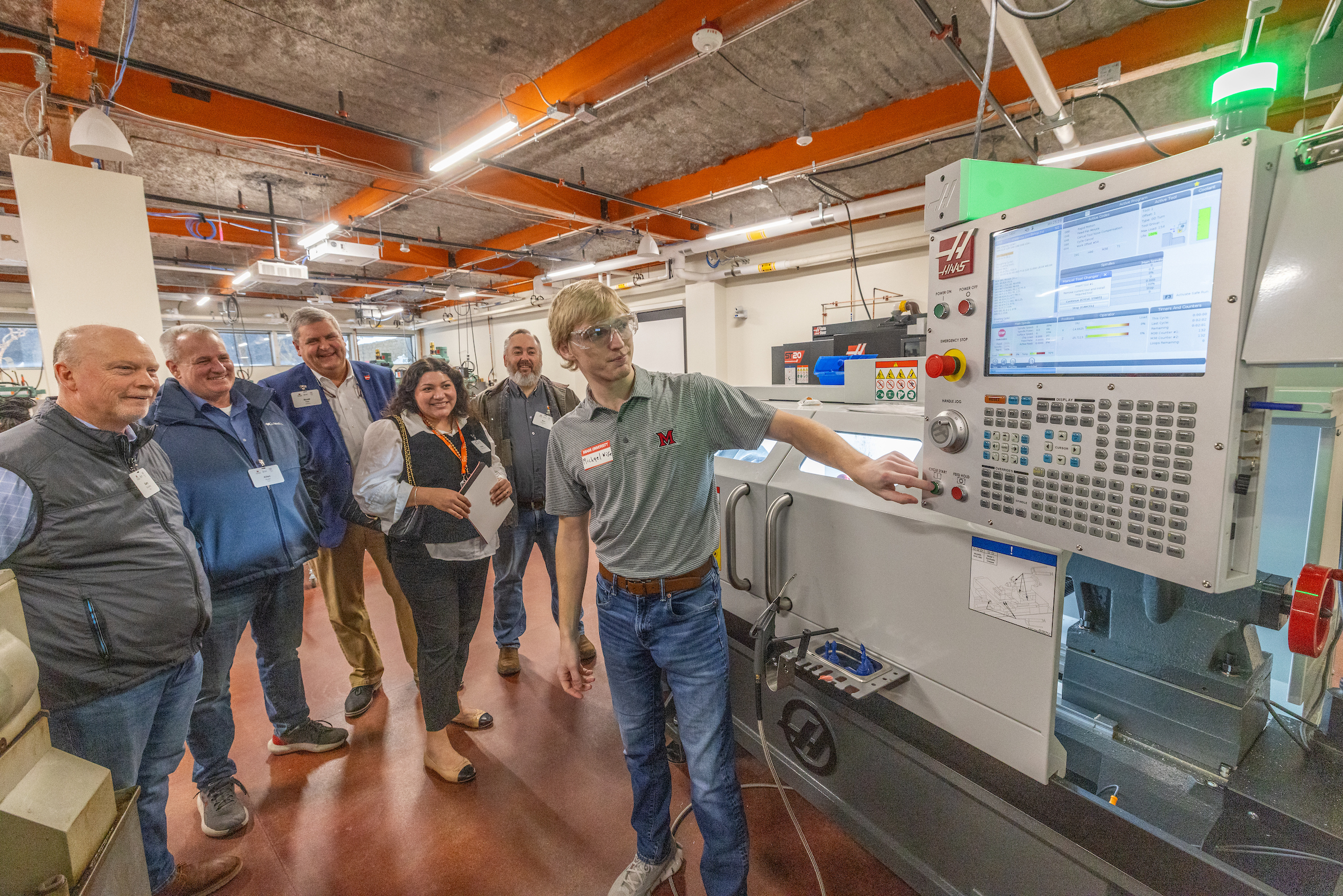 A student demonstrates a CNC machine to a group of adults at the MU AM ...