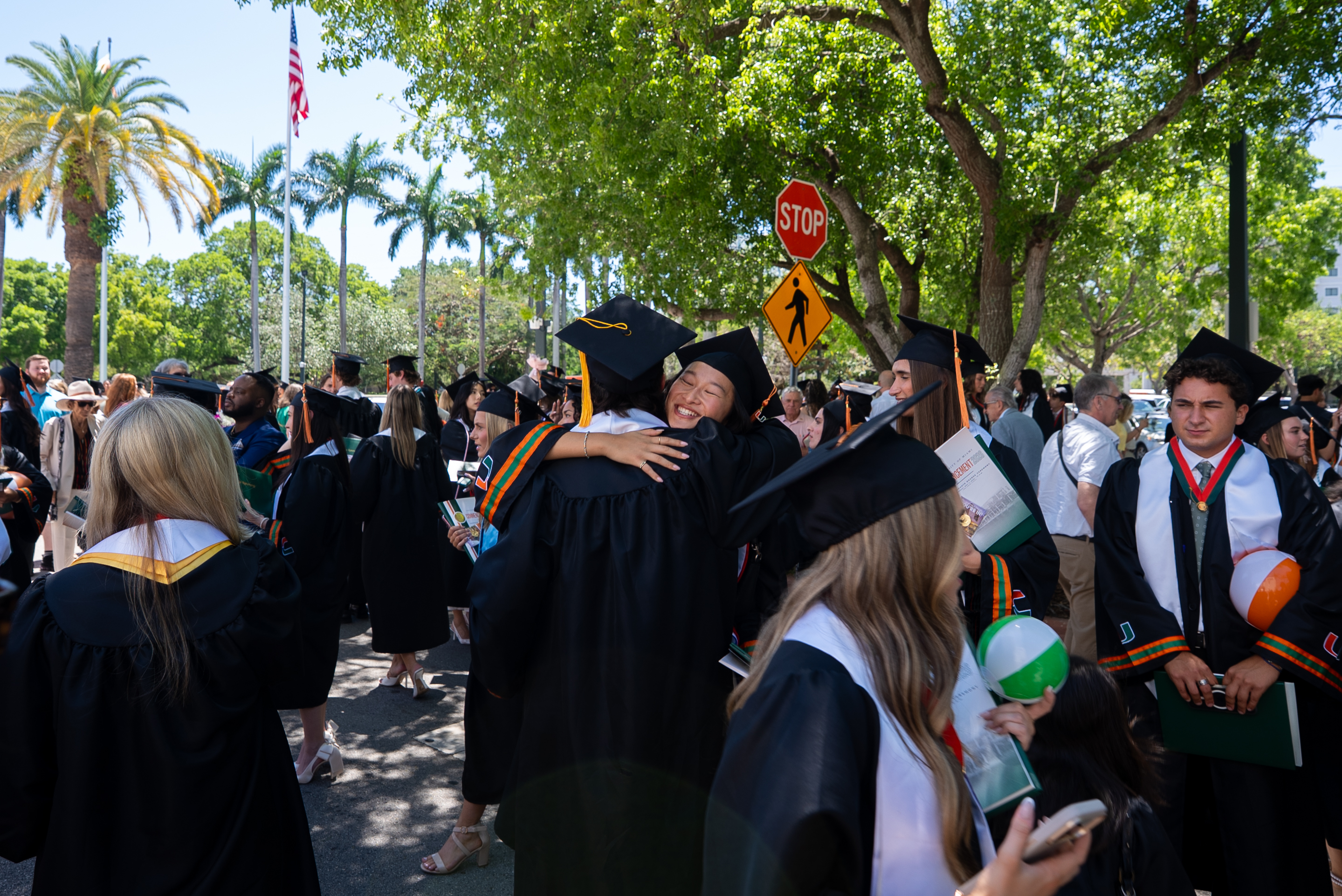 Graduates in caps and gowns embrace at an outdoor commencement ceremony ...