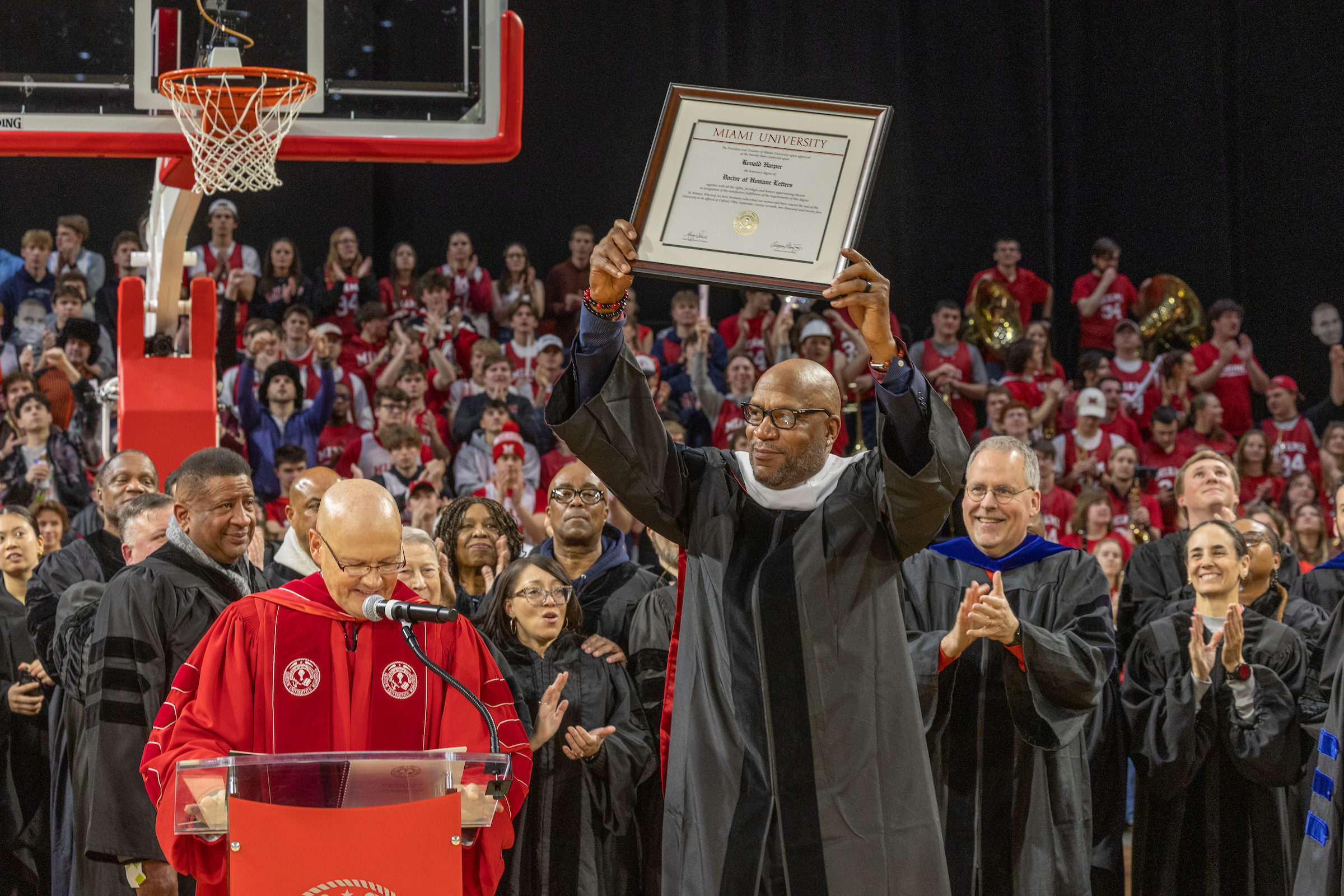 Ron Harper, in graduation gown, holds honorary degree above his head on ...