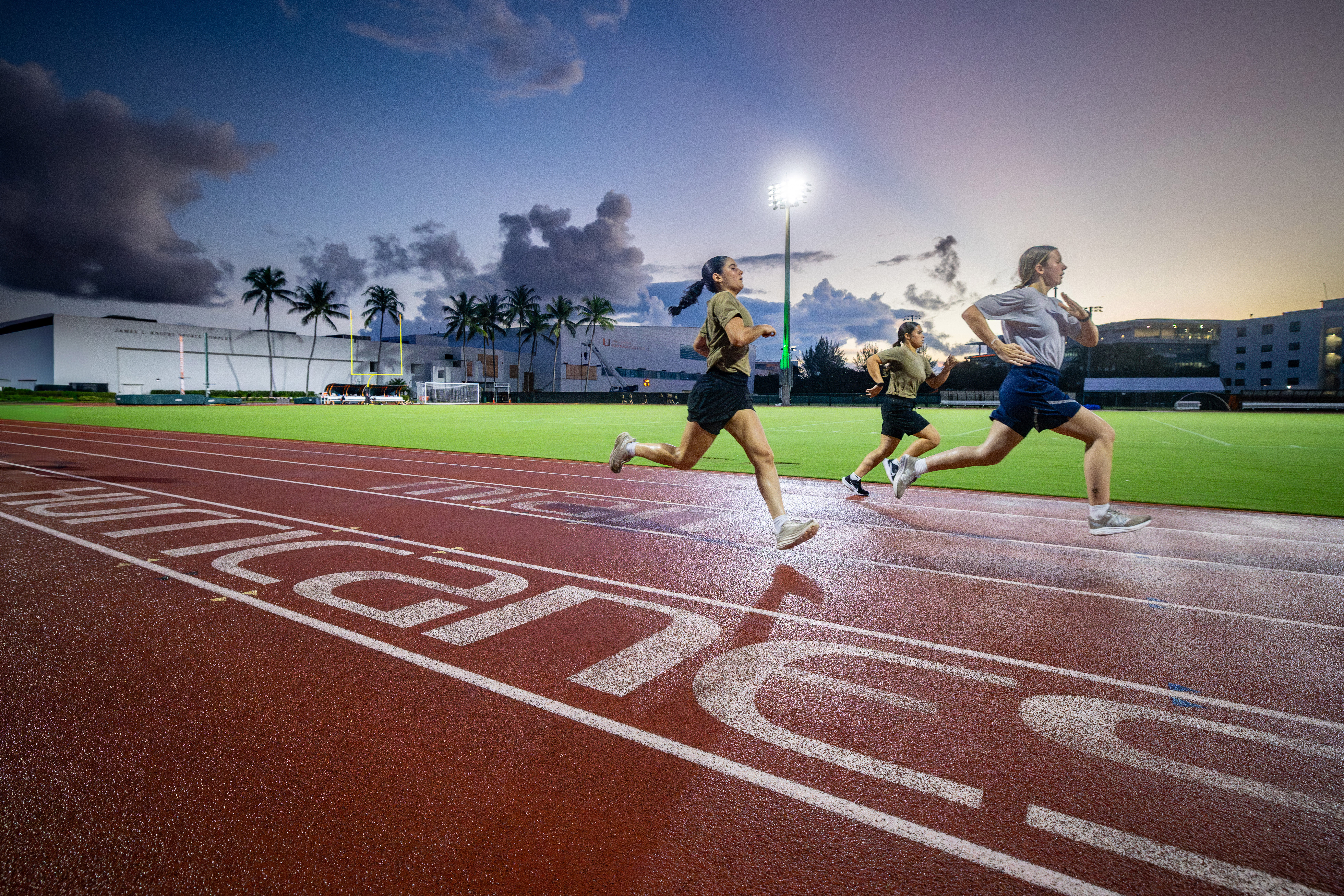 Three female athletes run on a track marked with