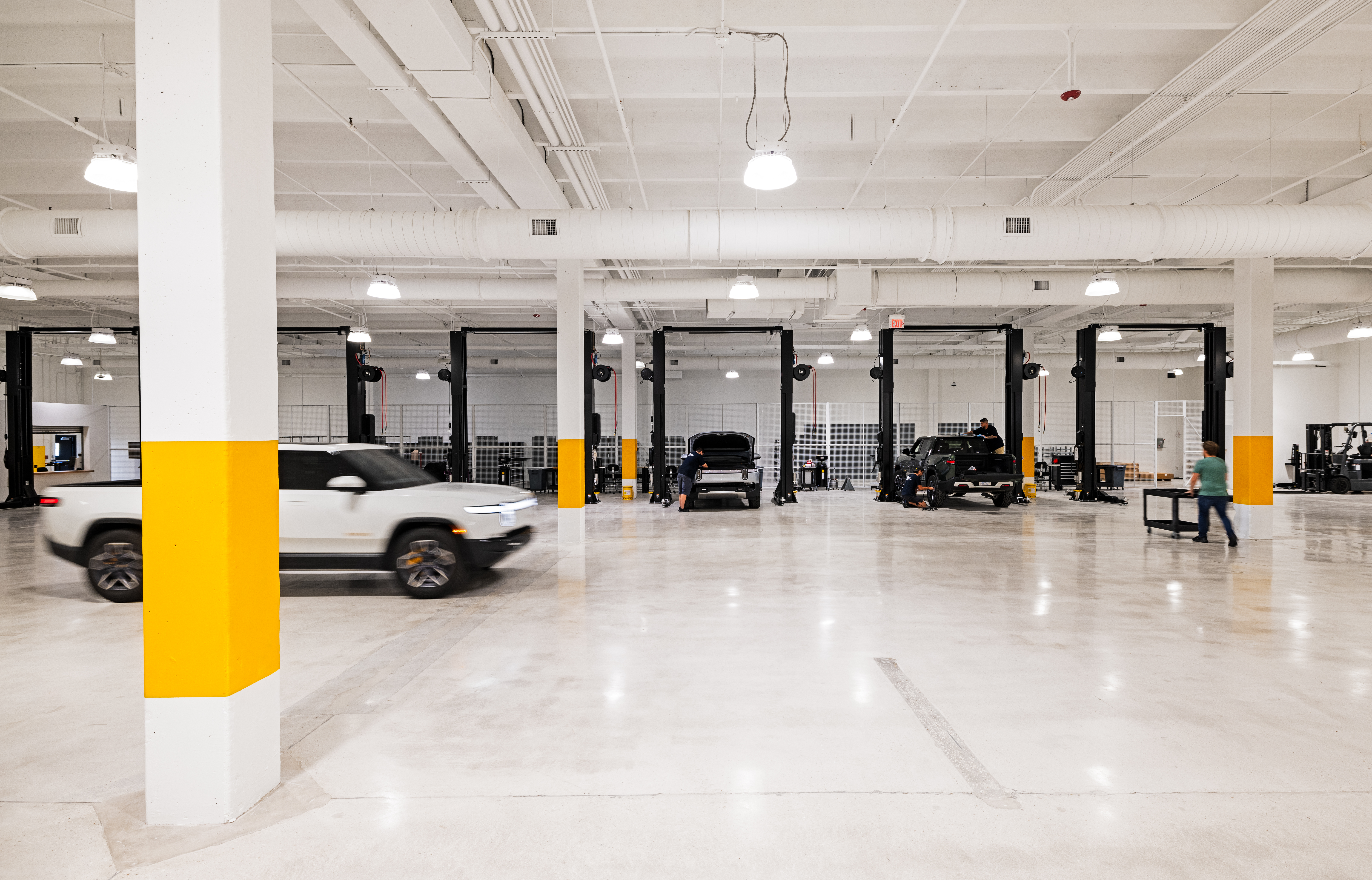 A white Rivian truck drives through a brightly lit service center with ...