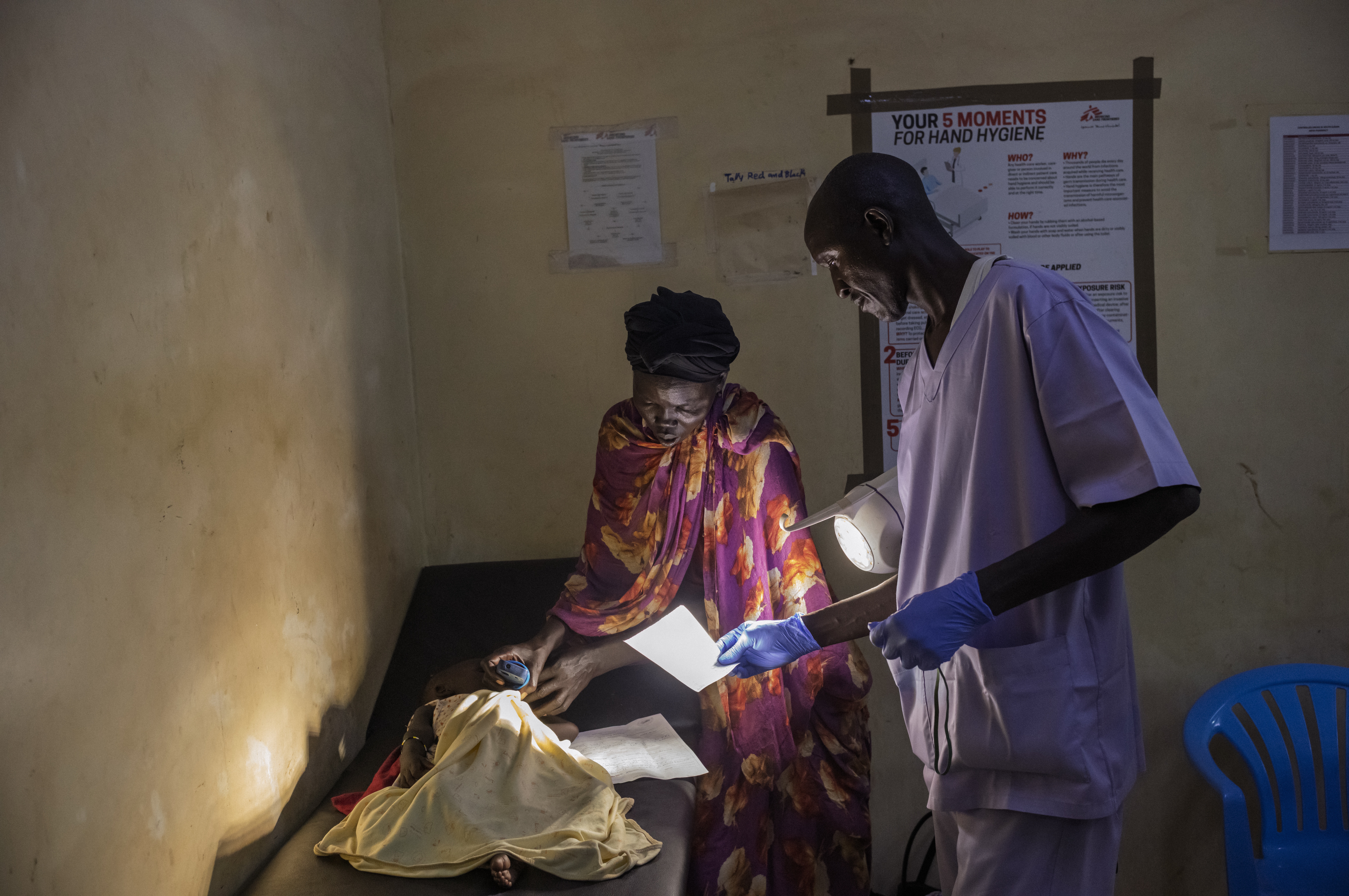 In a consultation room, an MSF nurse examines Thiany Chol under a ...