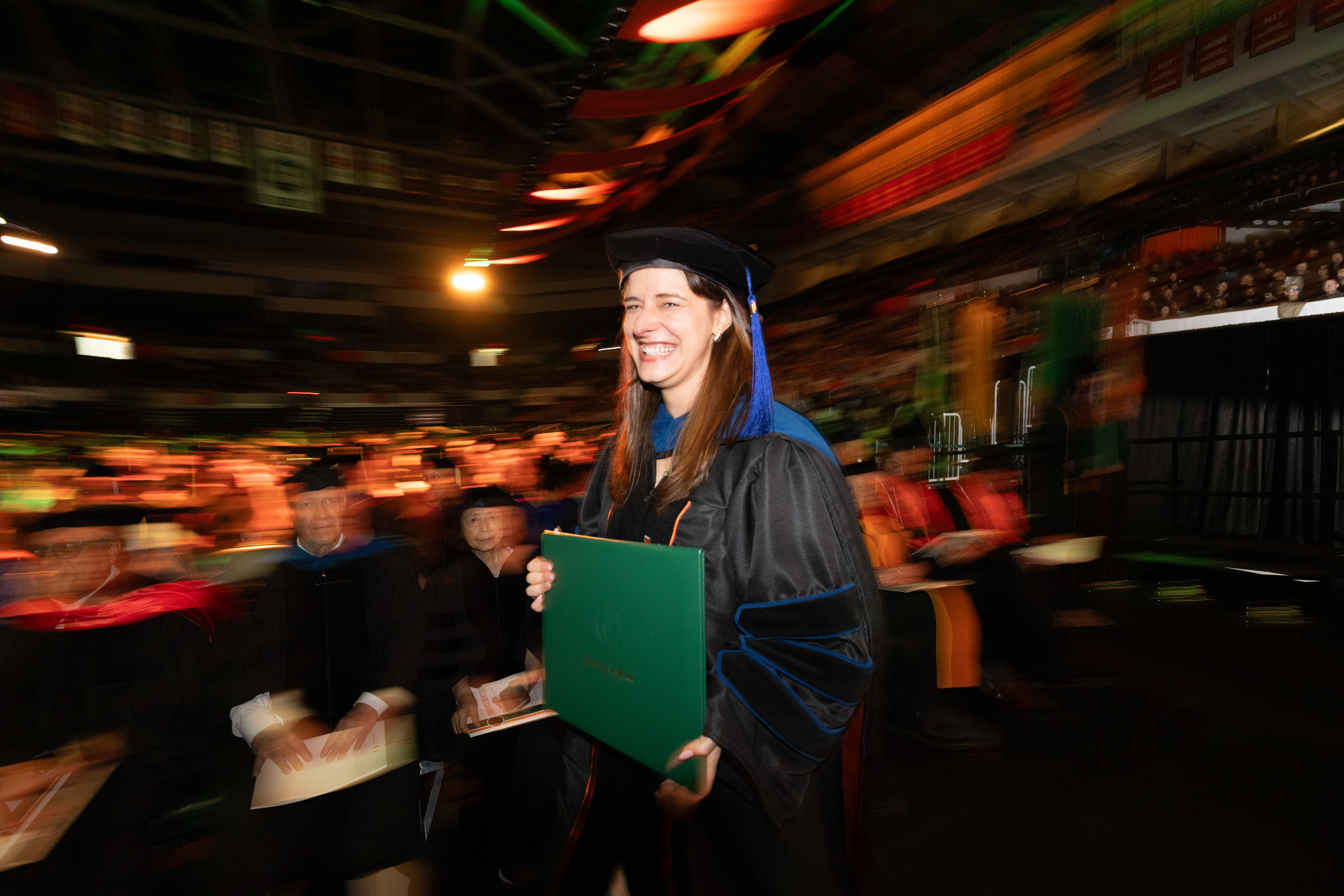 Smiling graduate in cap and gown walks with diploma at commencement ...